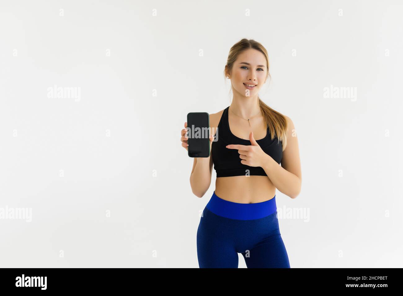 Attractive cheerful young fitness woman showing blank smartphone screen ...