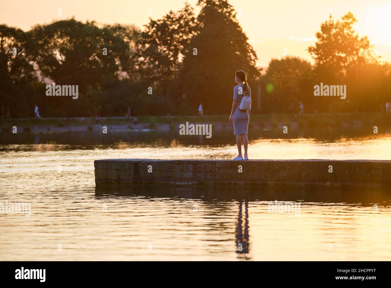 Back view of lonely woman standing on lake side on warm evening ...