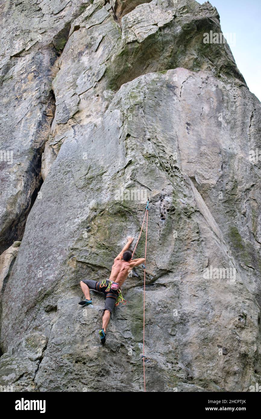 Determined climber clambering up steep wall of rocky mountain ...