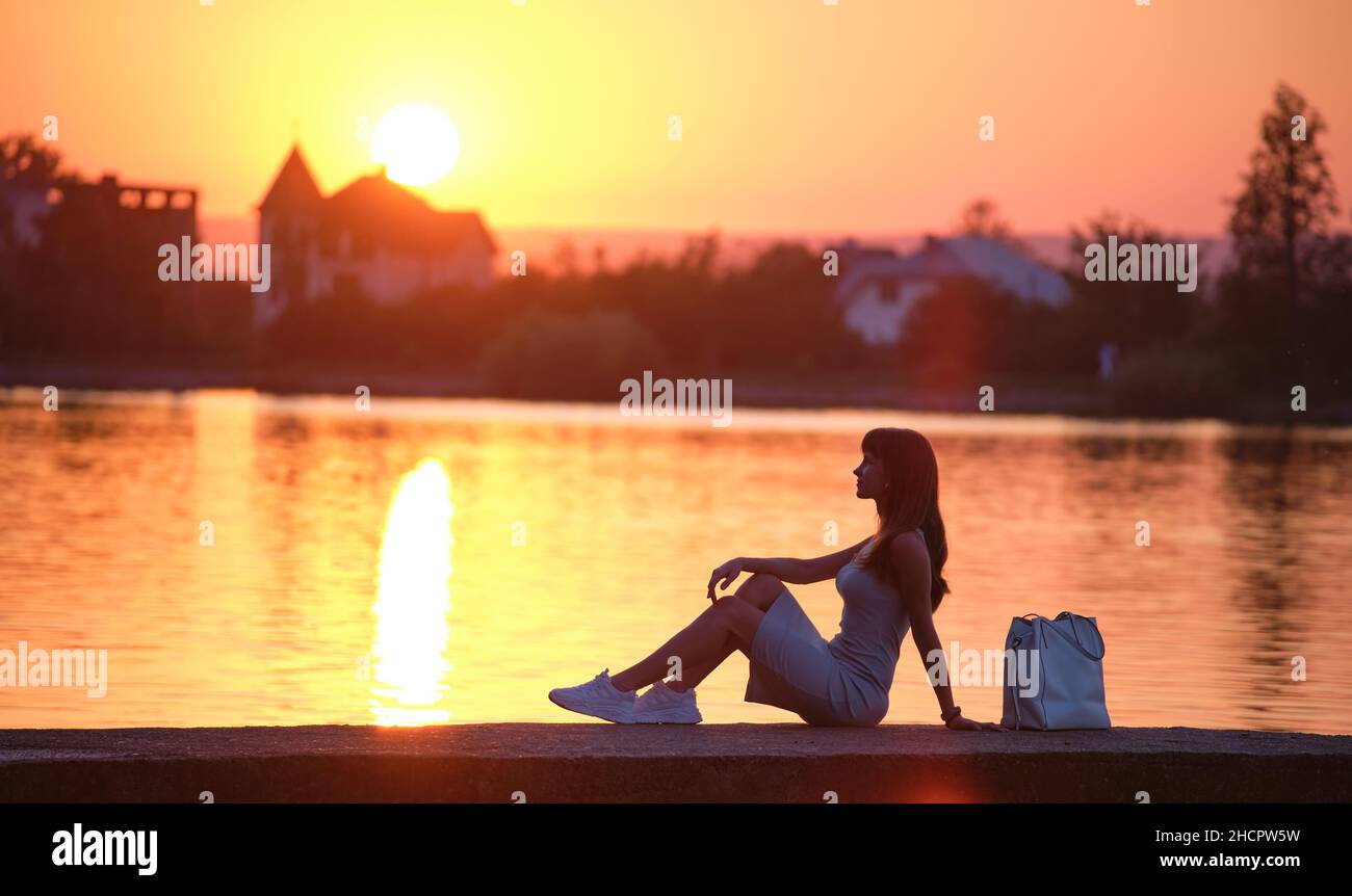 Lonely woman sitting alone on lake shore on warm evening. Solitude and ...