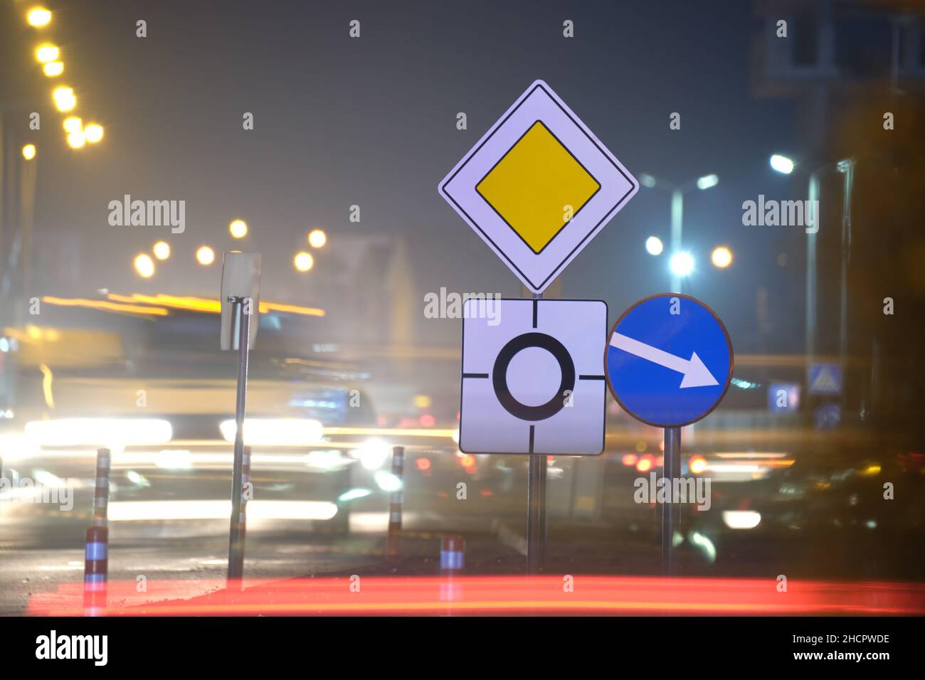 Roundabout road signs with blurred cars on city street traffic at night ...