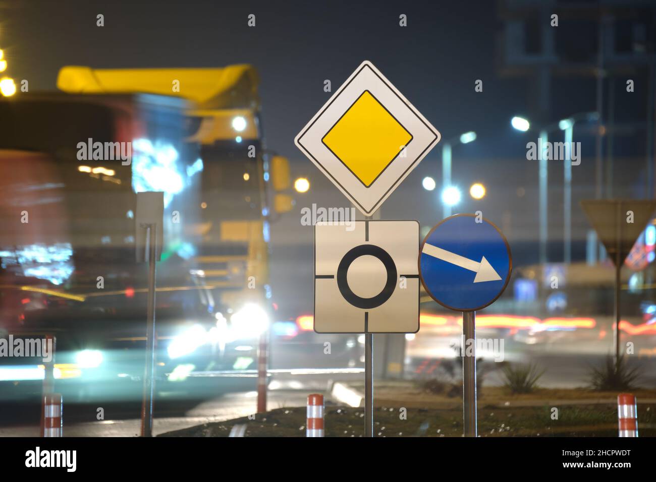 Roundabout road signs with blurred cars on city street traffic at night ...