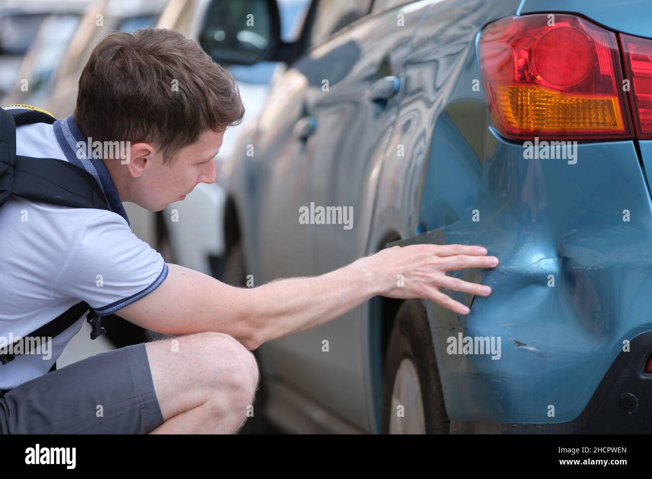 Sad male driver sitting on street side shocked looking at his dented ...