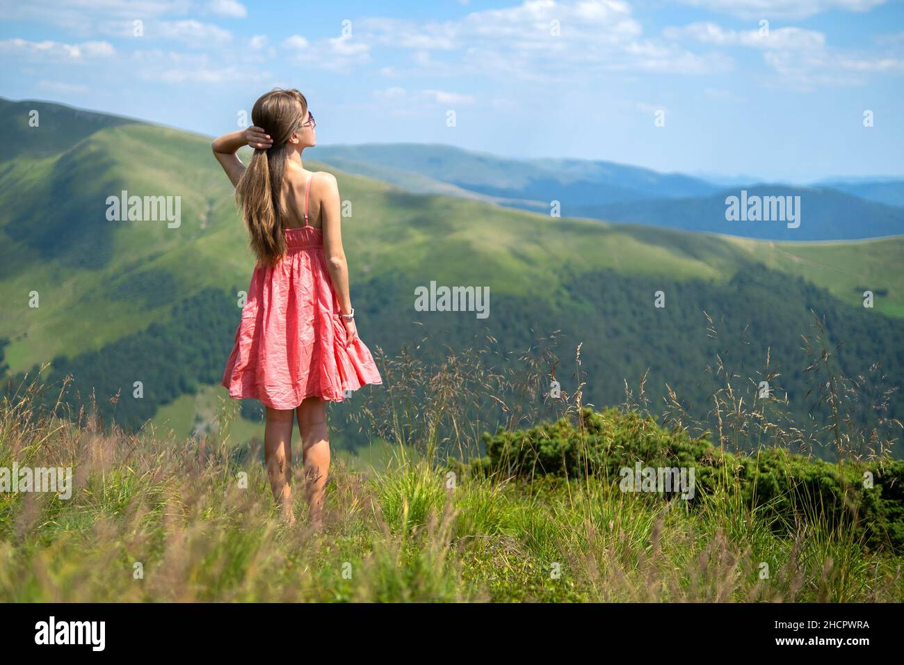 Young happy woman in red dress walking on hillside meadow on a windy ...