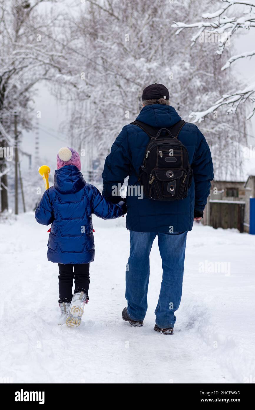 Dad and daughter go for a walk on a snowy road on a winter day. Winter ...