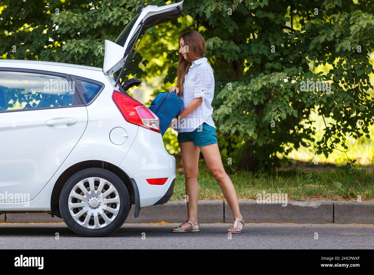 Young woman driver loading suitcase in the car trunk Stock Photo - Alamy