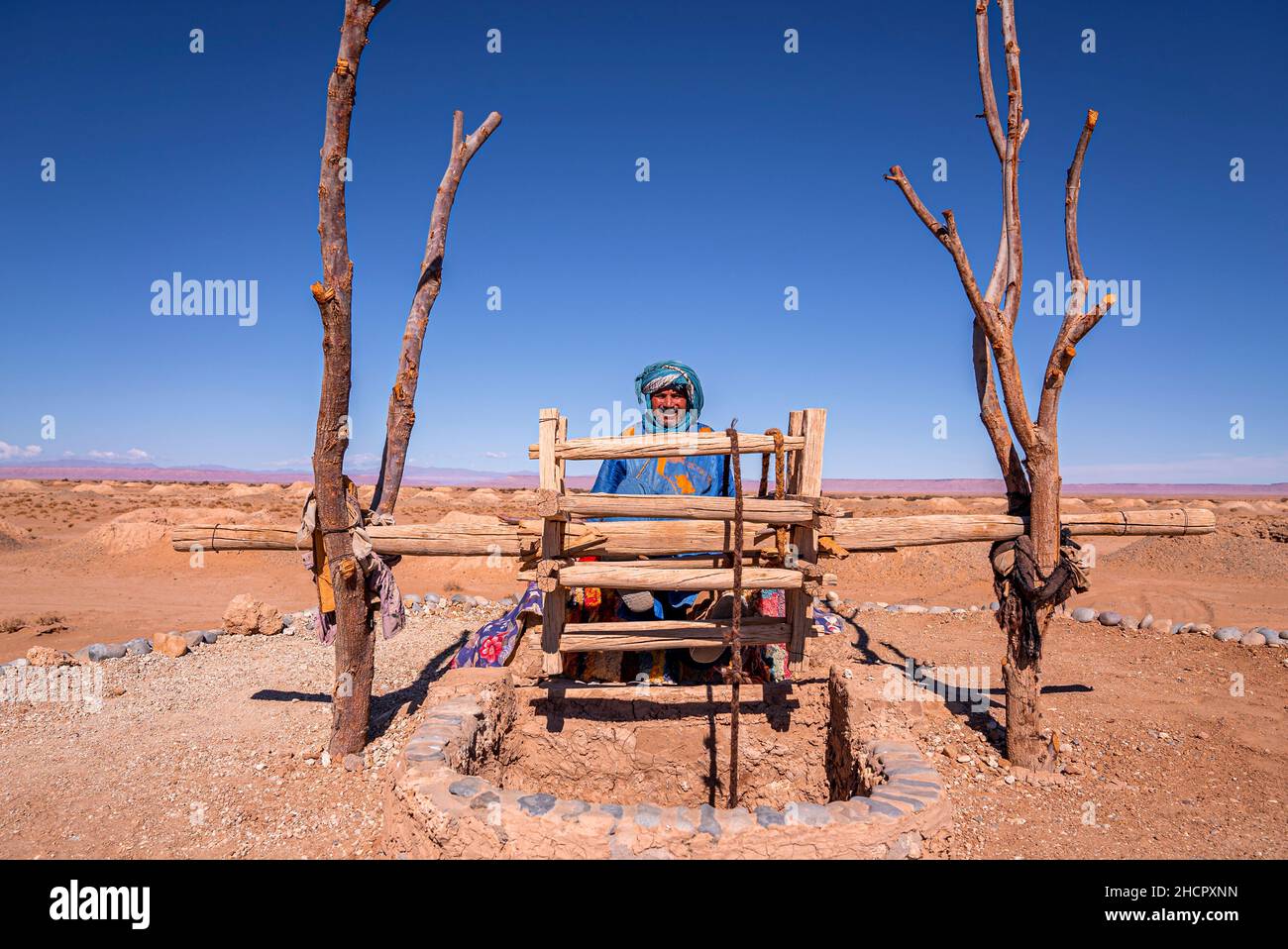 Man in traditional clothing taking out water from well using rope and ...