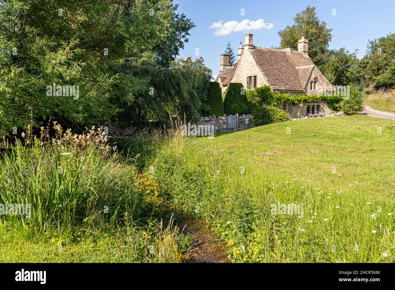 A traditional stone cottage beside the stream in the Cotswold village ...