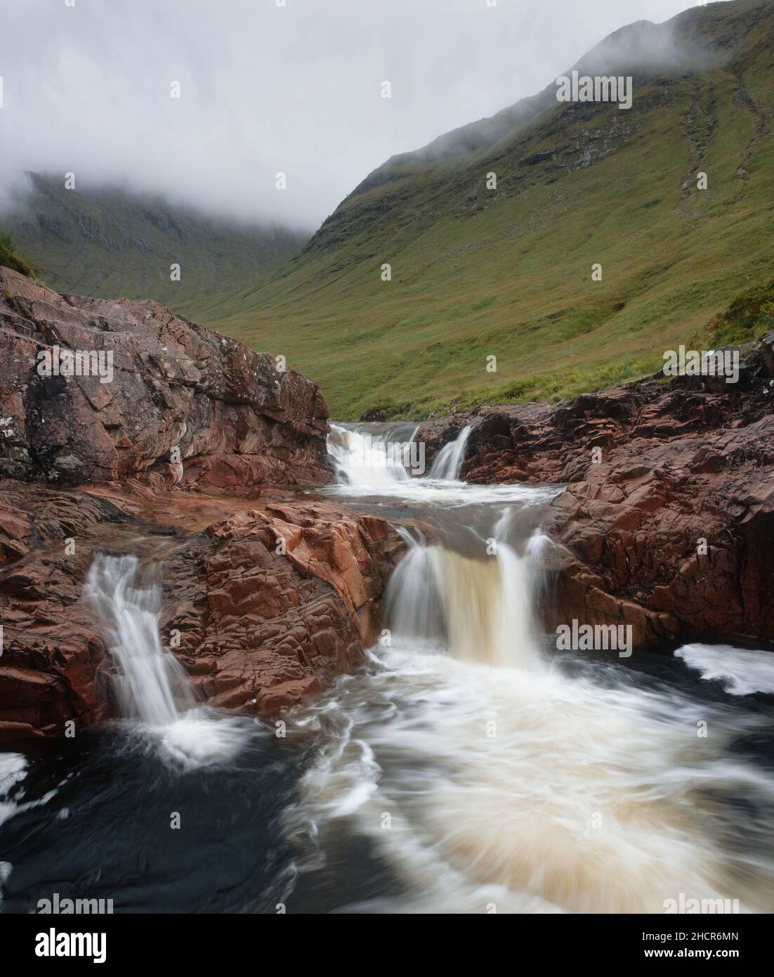 Small mountain river with waterfalls and mountains covered with clouds ...