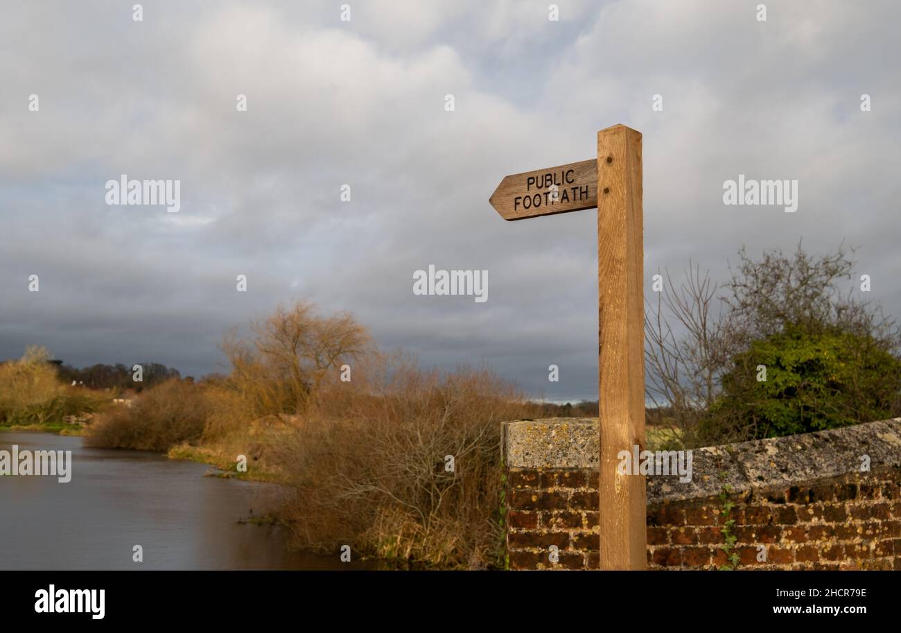 Wooden public footpath sign indicating public access along the bank of ...