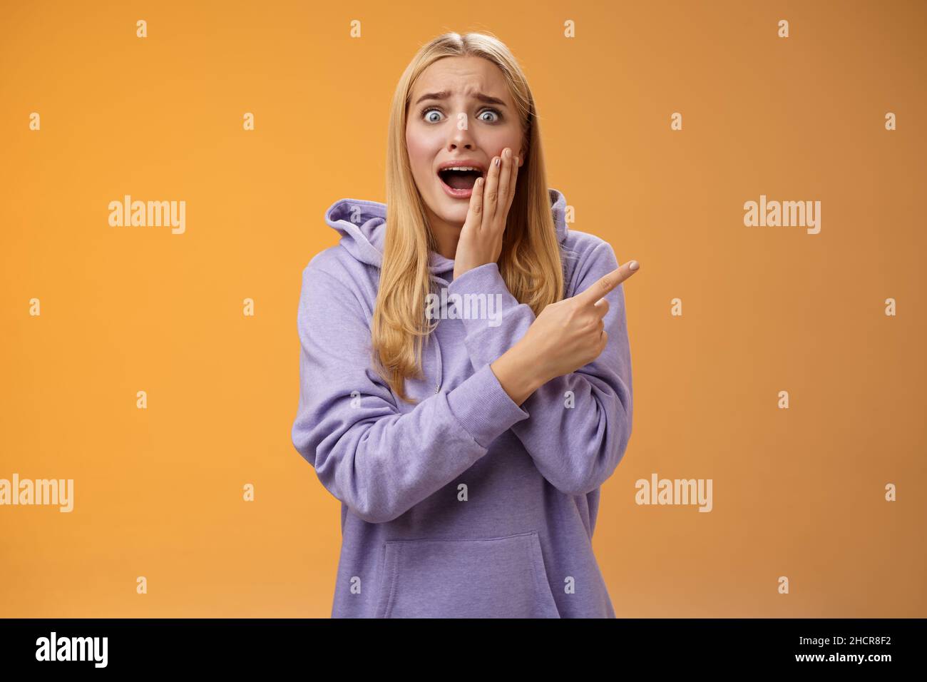 Amazed excited overwhelmed young blond girl in hoodie press palm cheek ...