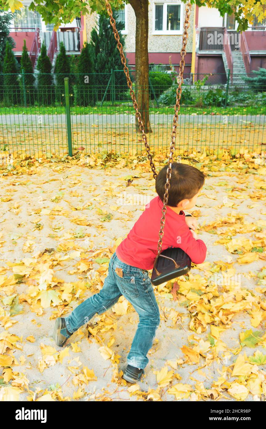 Vertical shot of a Caucasian kid playing in a playground with swing ...