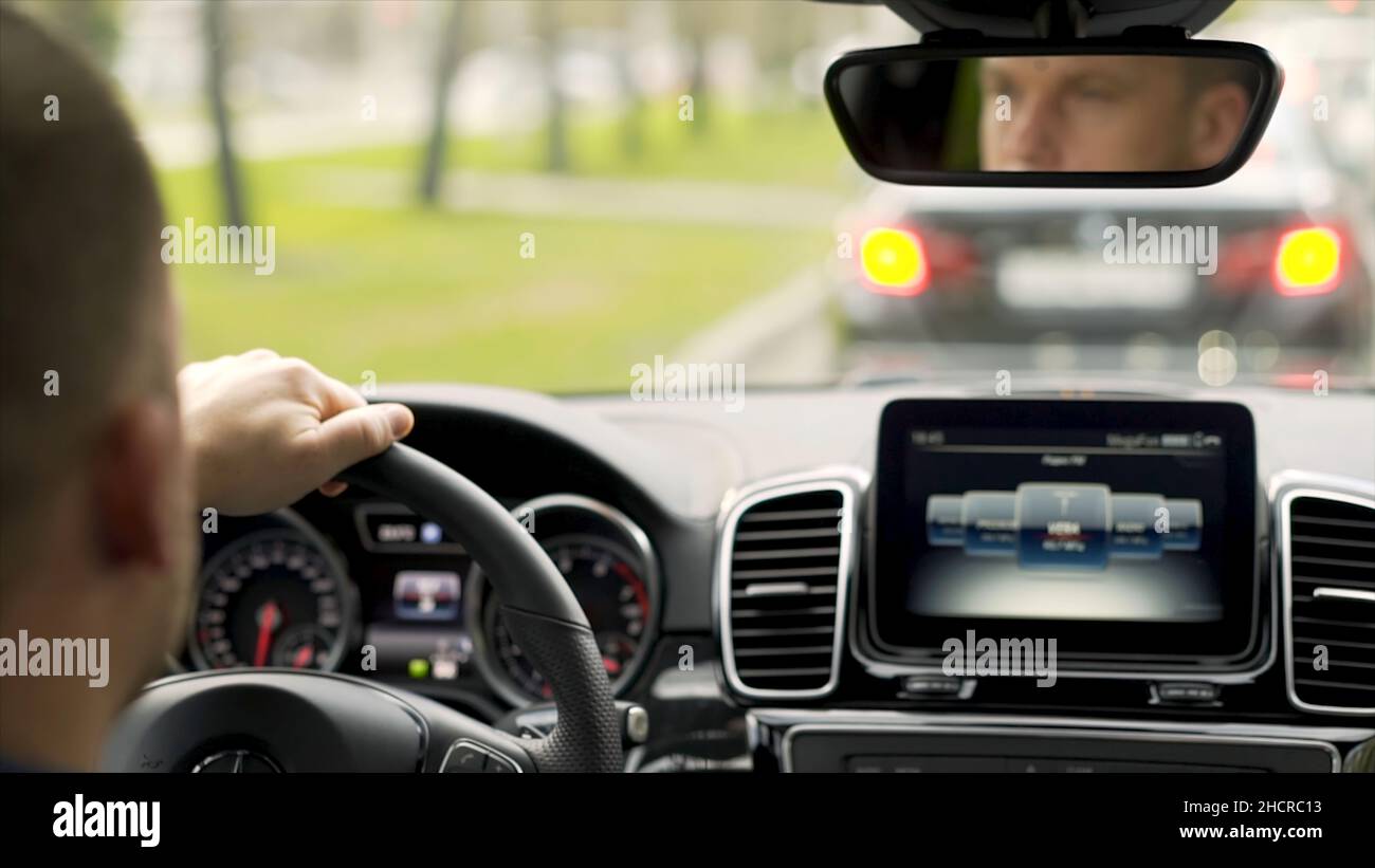 Man driving car from rear view in the city street along green trees ...