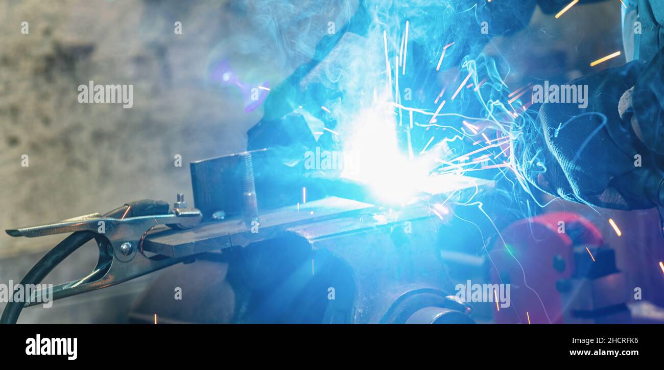 welder welds a metal piece and sparks from welding fly in different ...