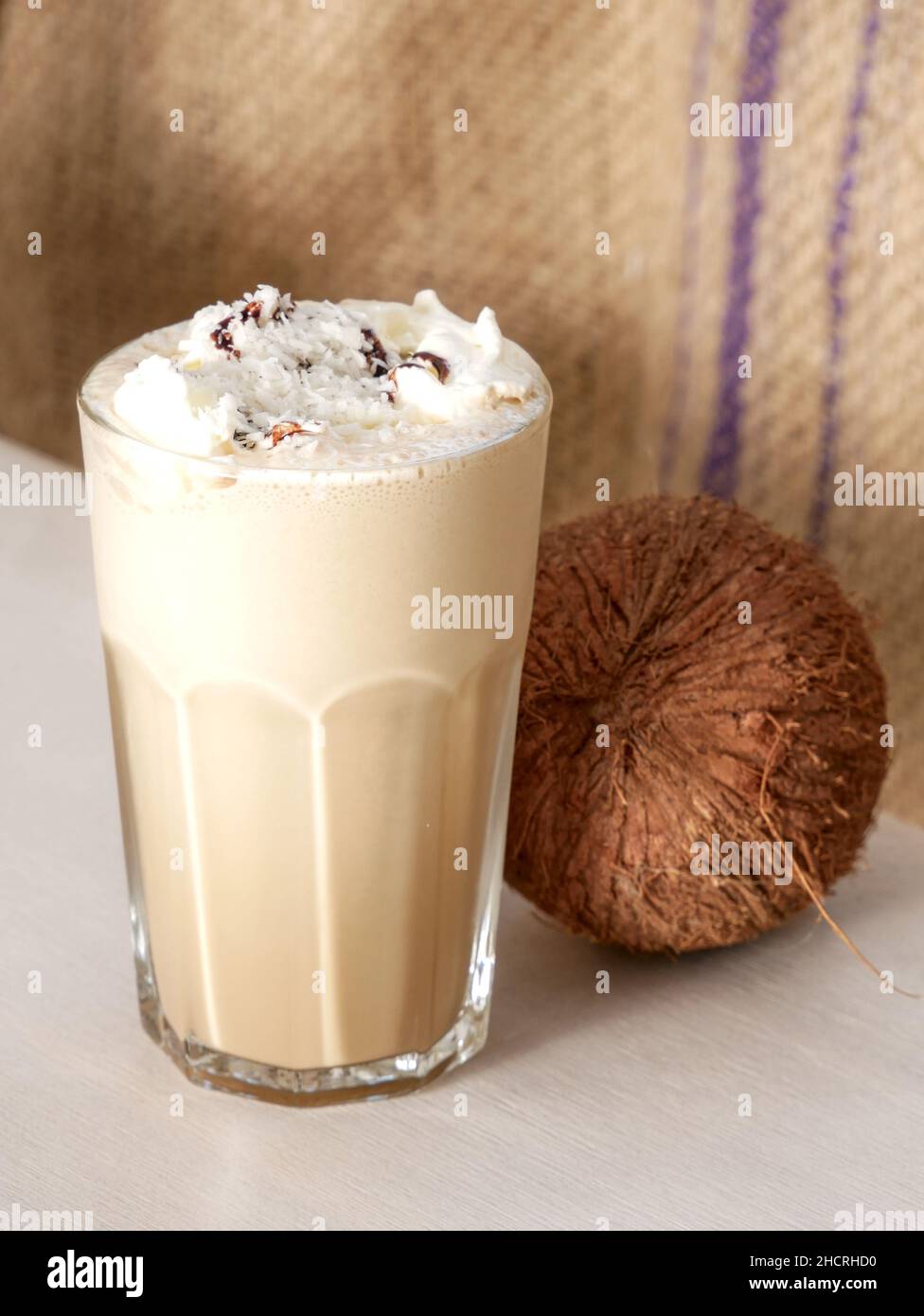 Coconut latte in a tall glass and coconut on a swing in a cafe. Close ...