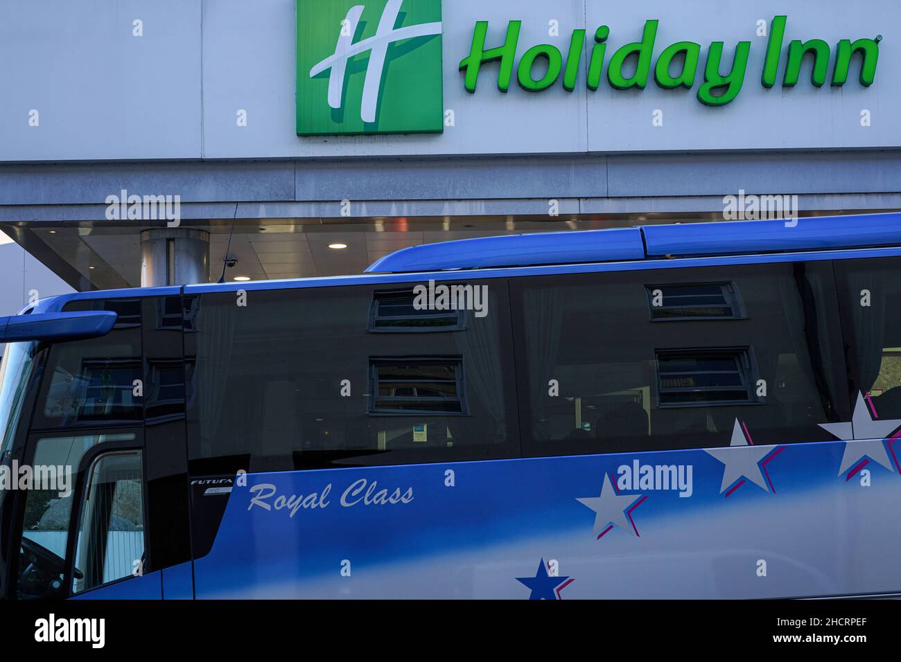 A blue coach is parked in front of a hotel of the Holiday Inn Group ...