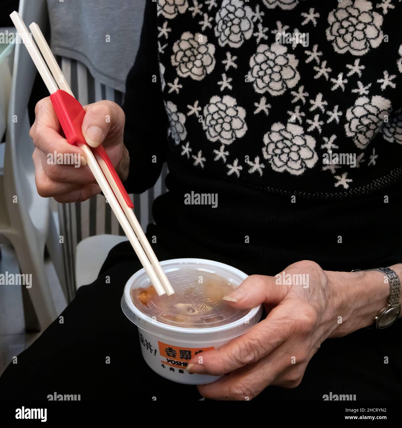 An elderly woman with arthritis in her hands using special chopsticks ...