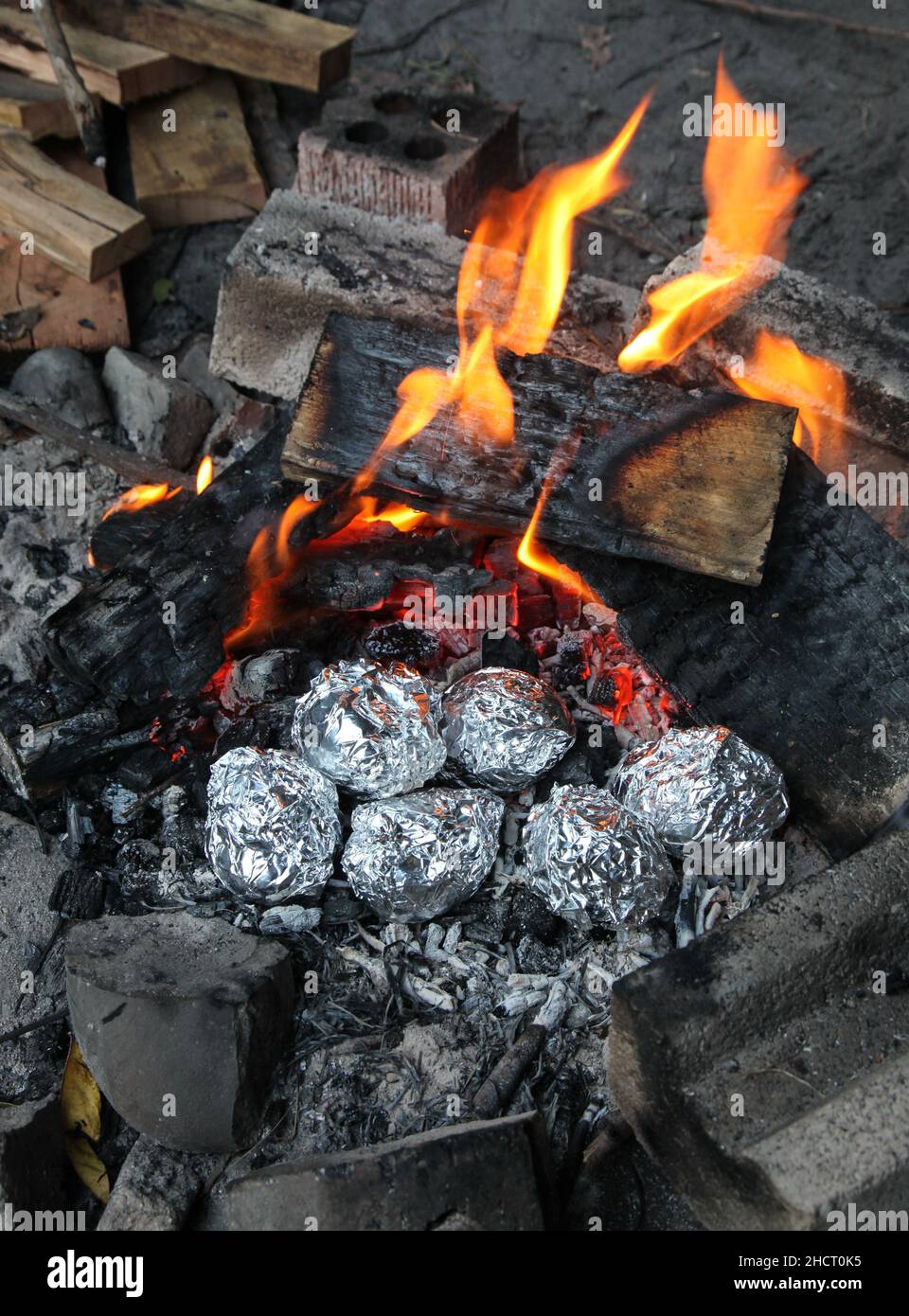 A camp fire with potatoes roasting in aluminium foil in the hot coals ...
