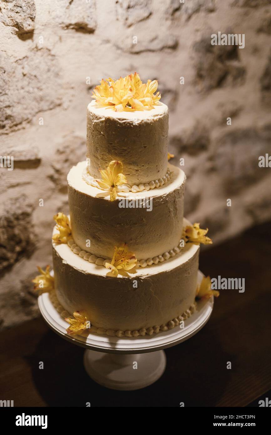 Three-tiered wedding cake on a rotating stand against a white stone ...
