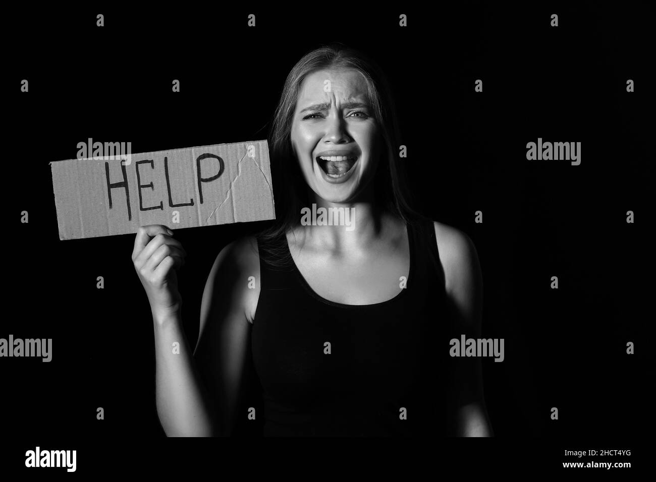 Scared woman holding paper with word HELP on dark background. Violence ...