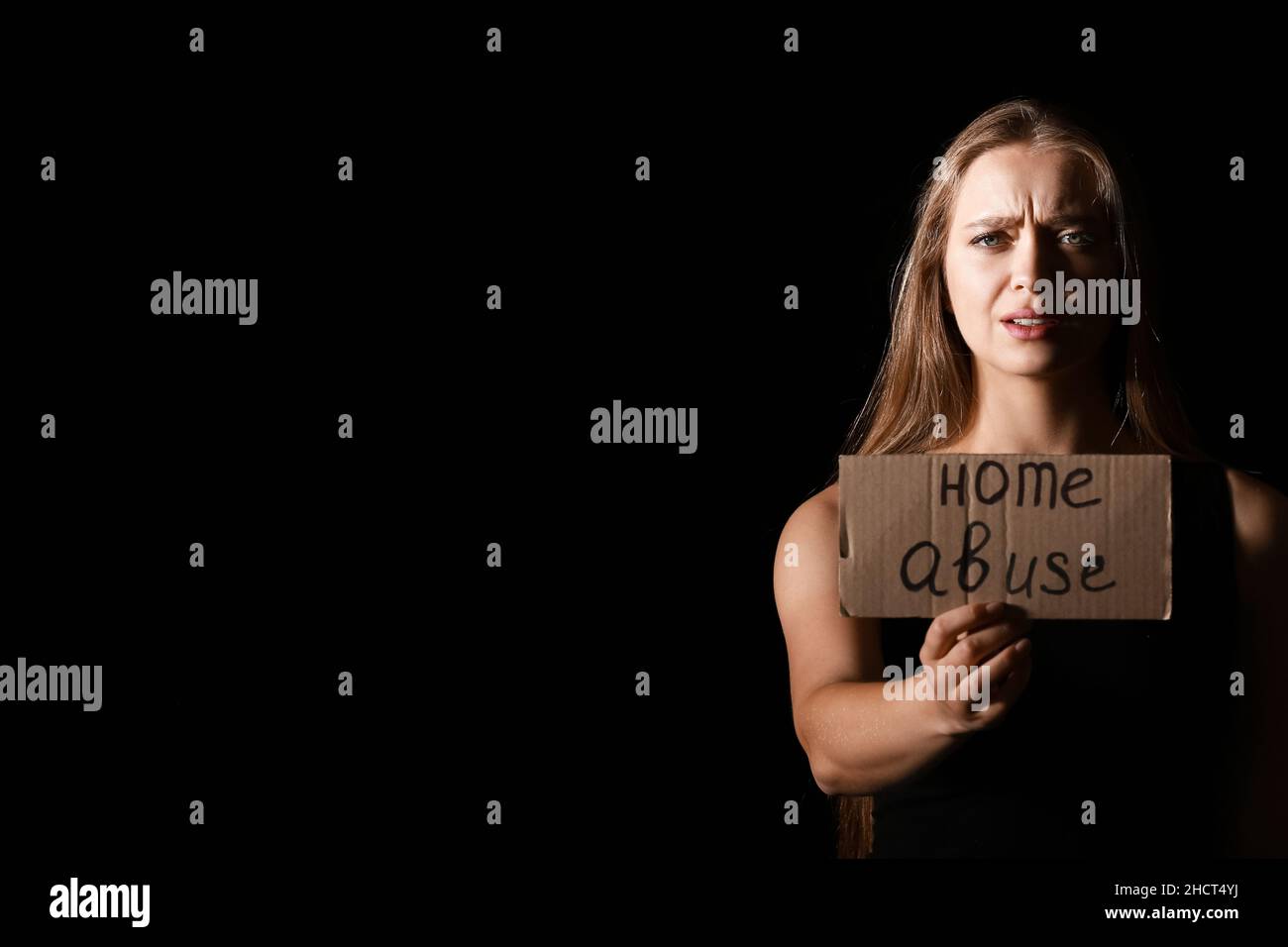 Scared woman holding paper with text HOME ABUSE on dark background ...