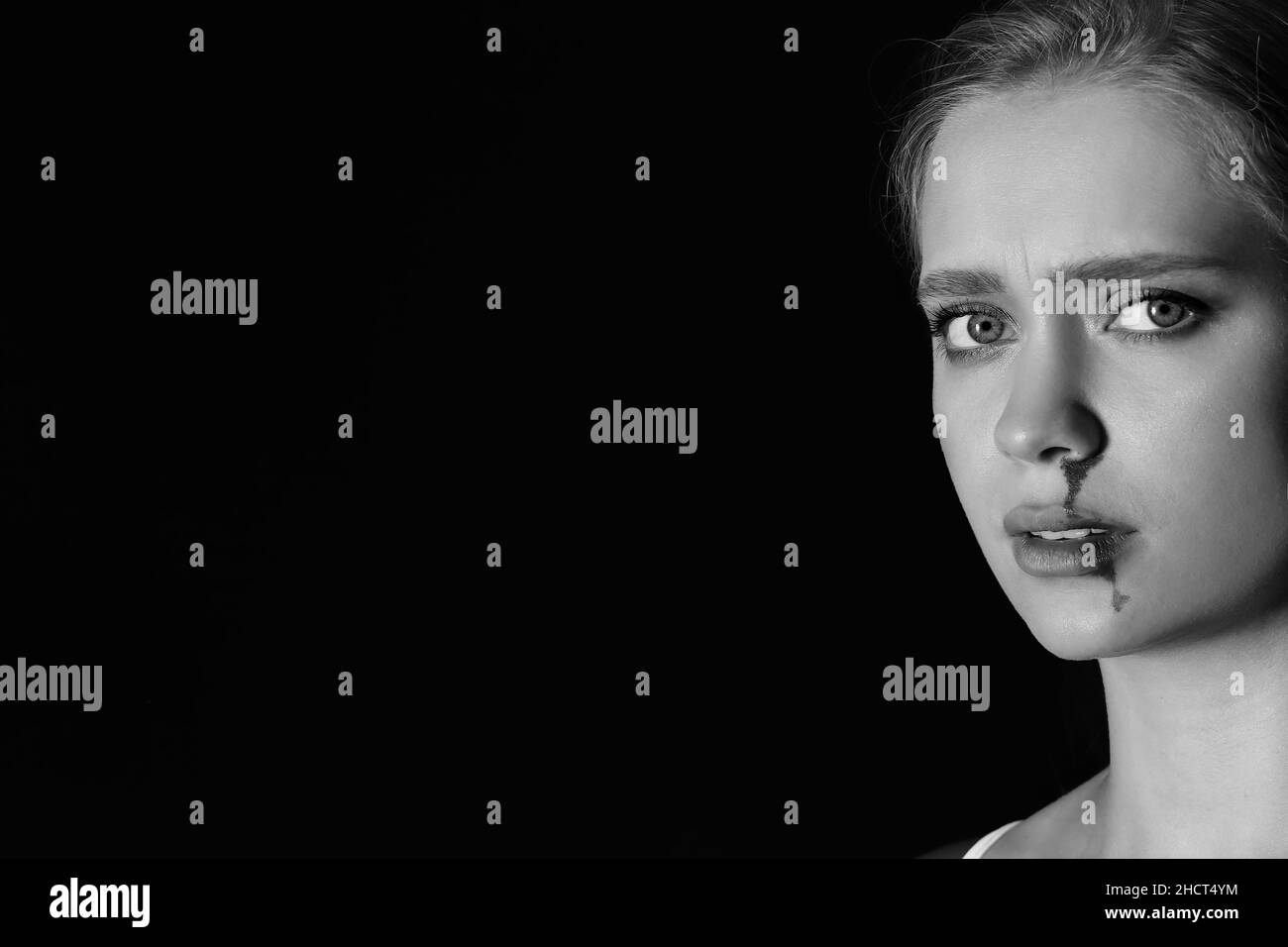Scared woman with blood on her face against dark background. Violence ...