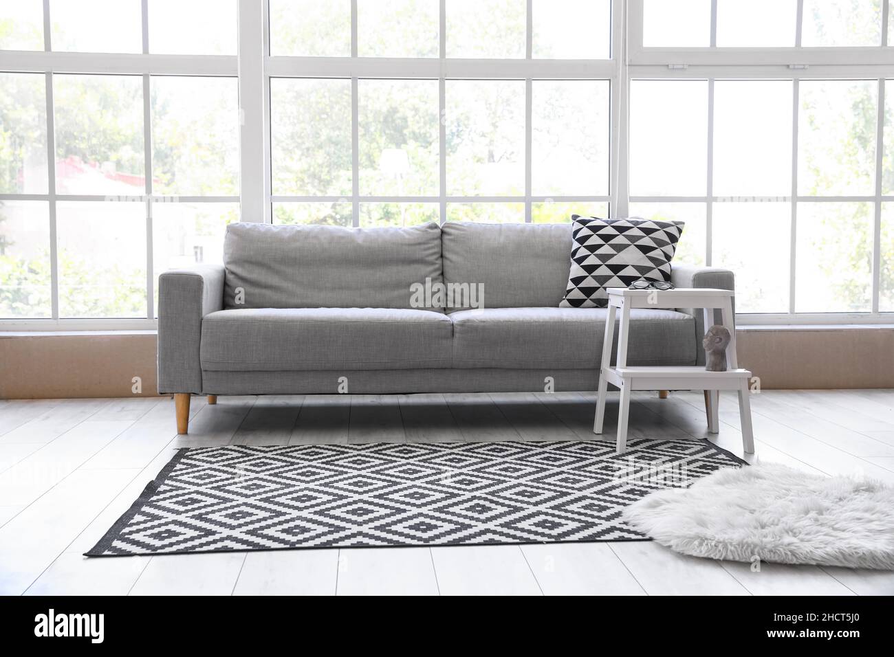 Grey sofa and white step stool near window Stock Photo - Alamy