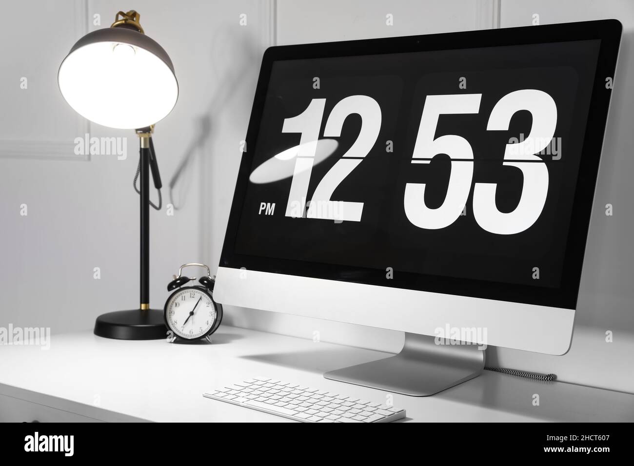 Modern computer, alarm clock and glowing lamp on desk in office Stock ...