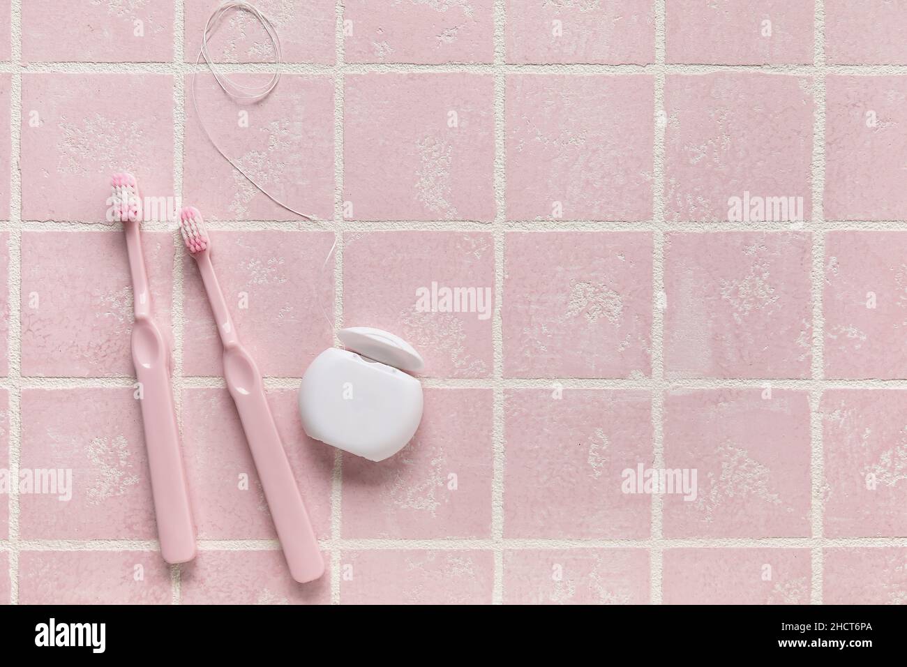 Dental floss with tooth brushes on pink tile background Stock Photo - Alamy