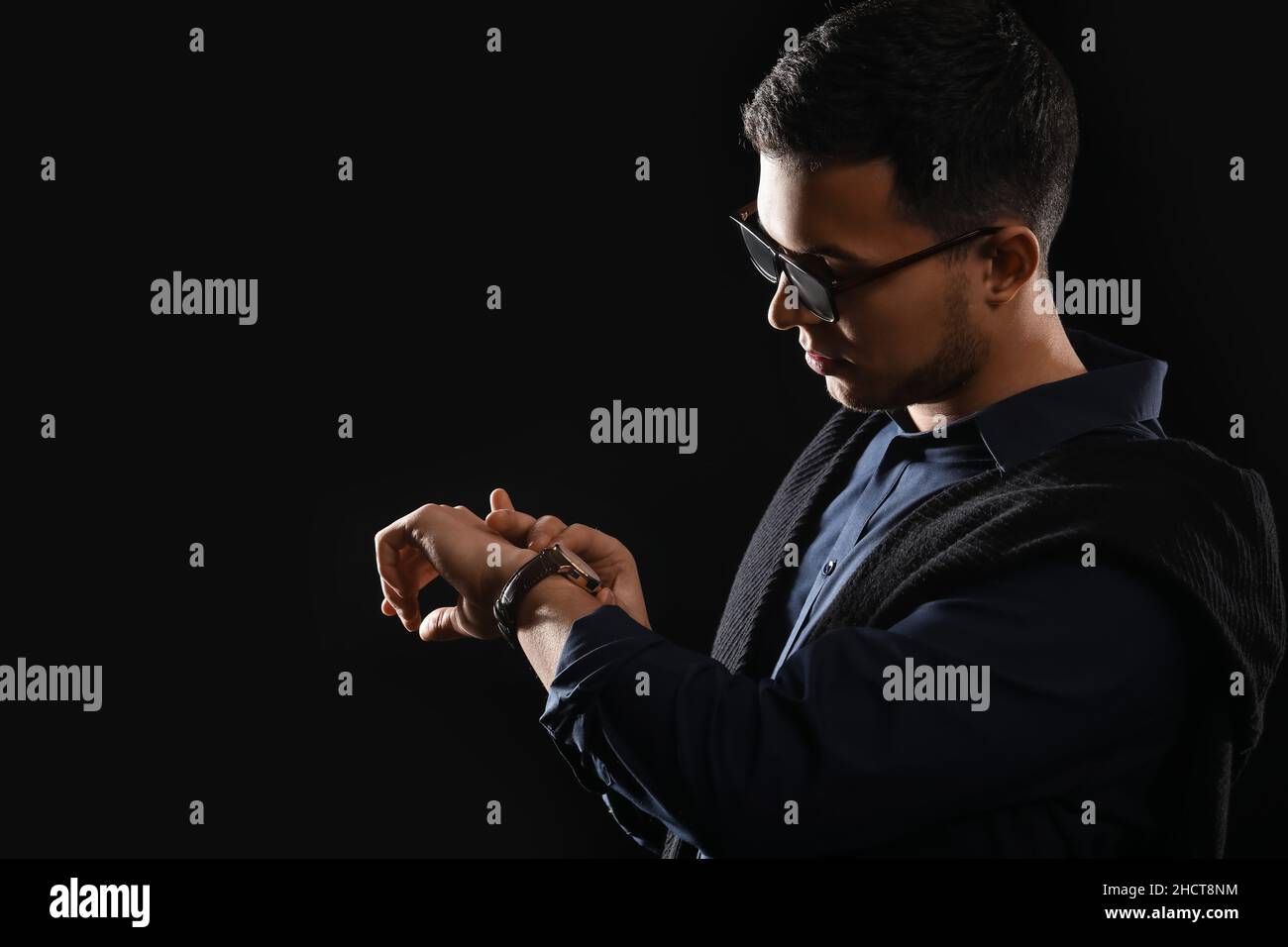 Portrait of handsome young man looking at wrist watch on black ...