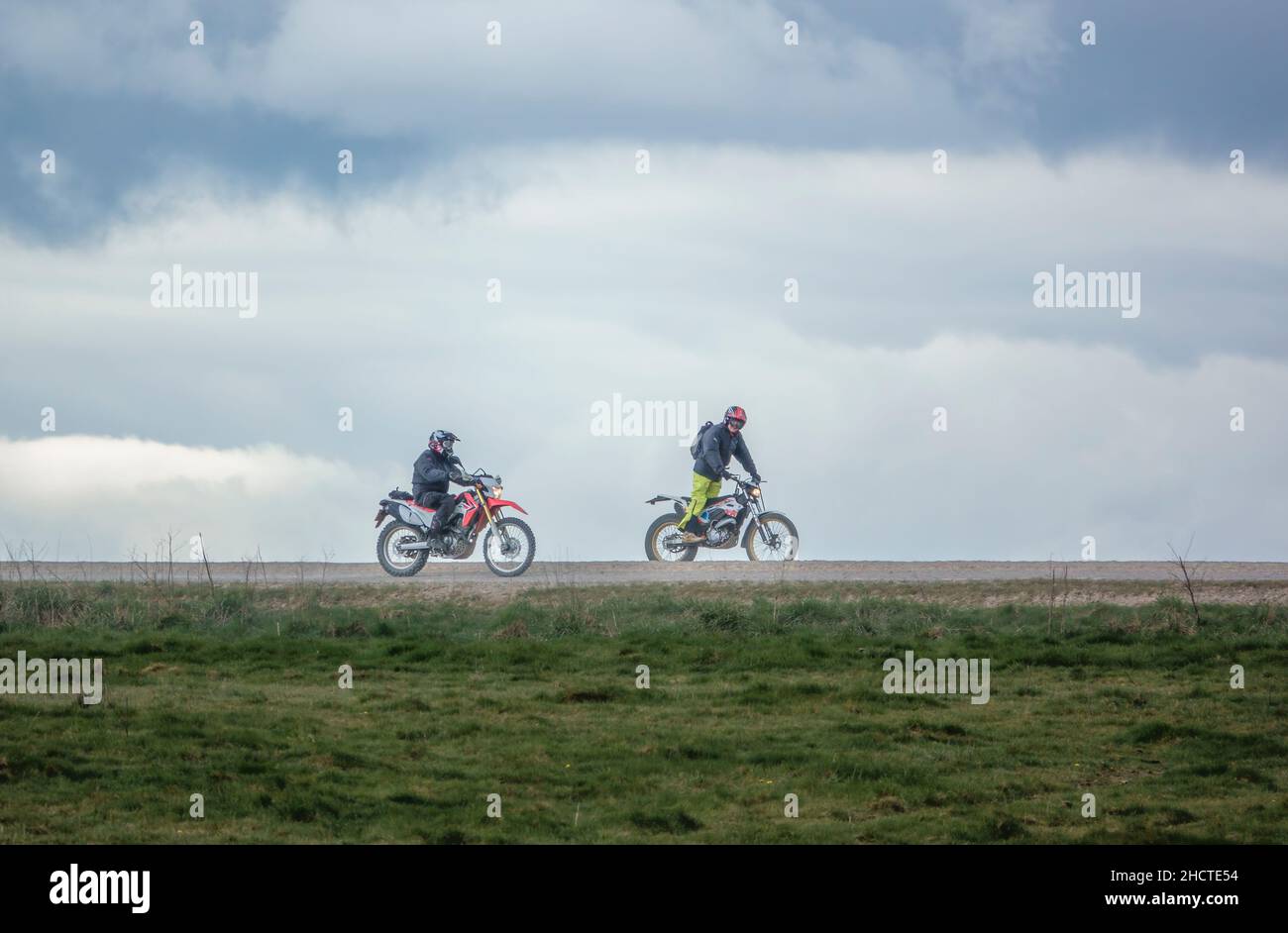 a pair of motorcyclists riding motorbikes across an unmade stone track ...