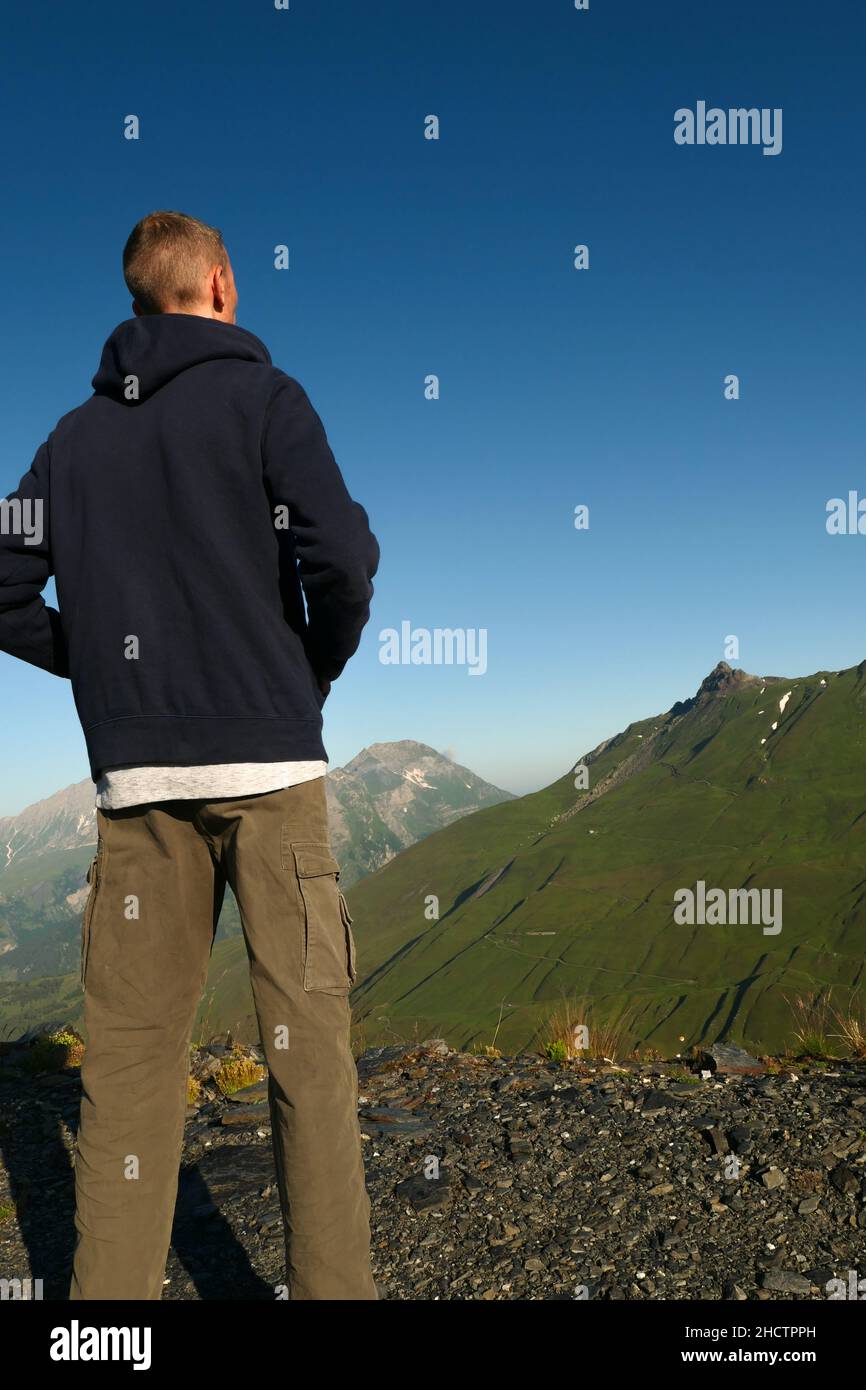A man from the back, facing green mountains. A hiker contemplates the ...