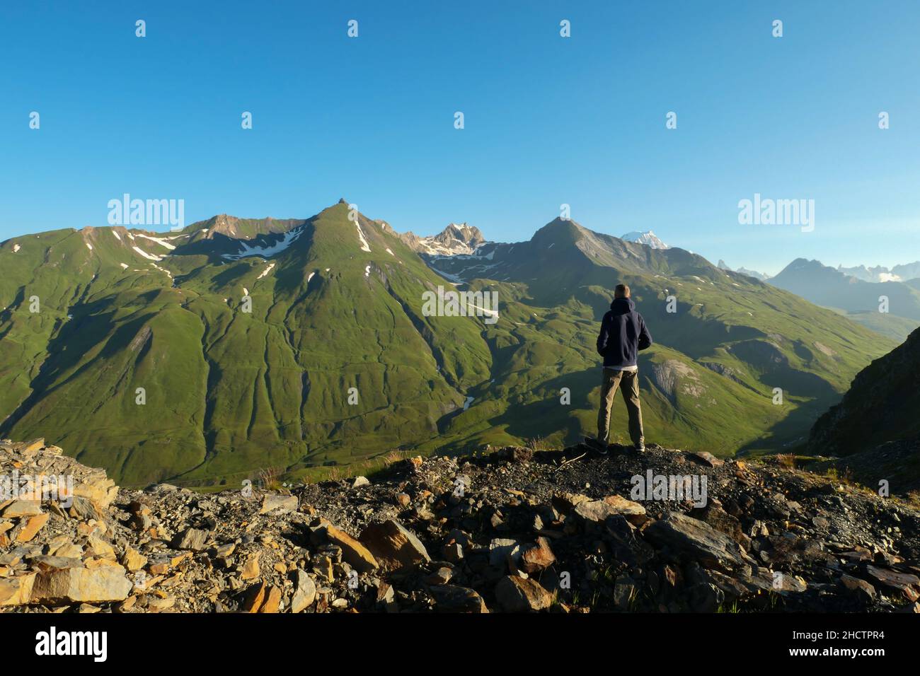 A man from the back, facing green mountains. A hiker contemplates the ...