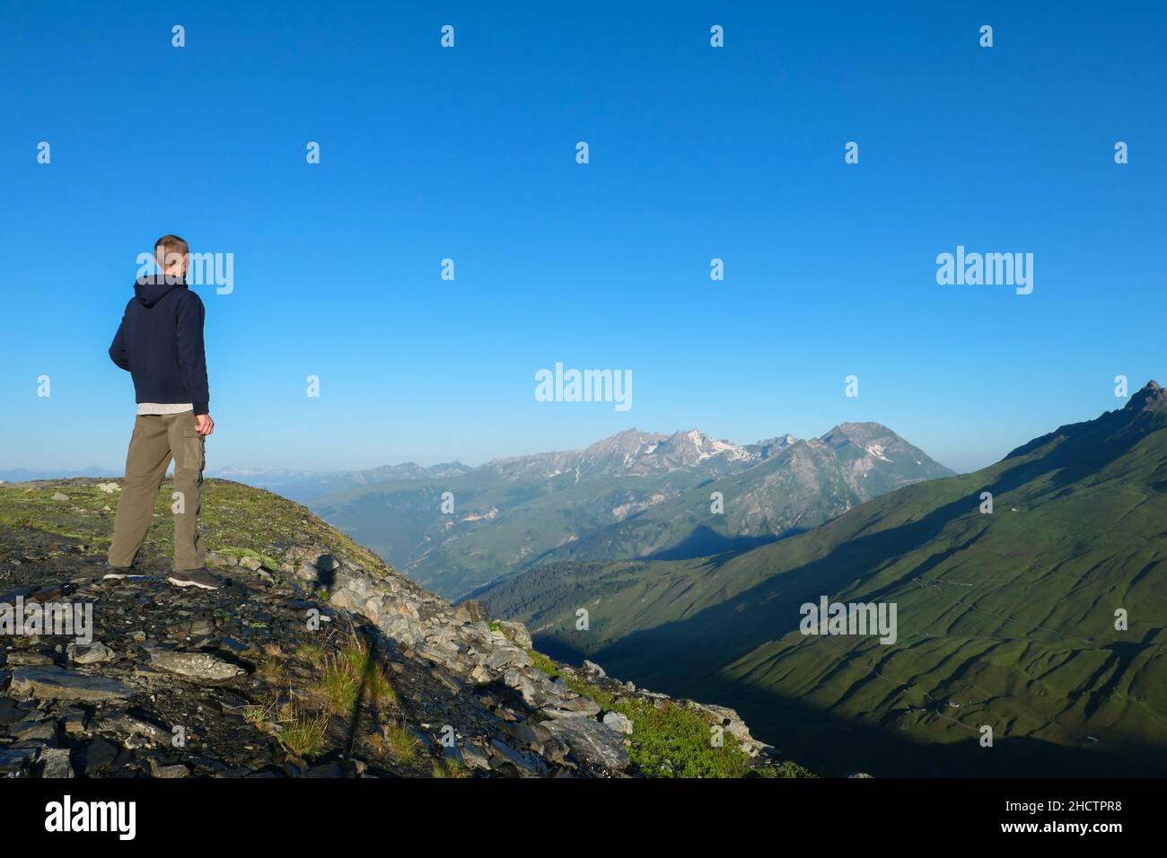 A man from the back, facing green mountains. A hiker contemplates the ...