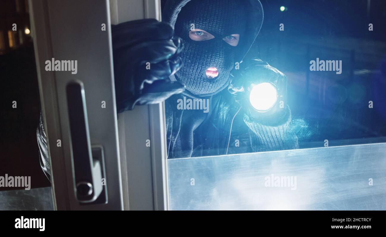 masked Burglar looking through window with flashlight at night Stock ...