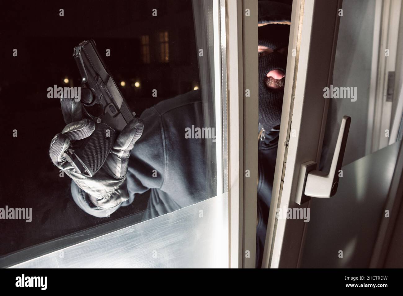 Burglar with gun looking at a window to breaking and entering a victim ...