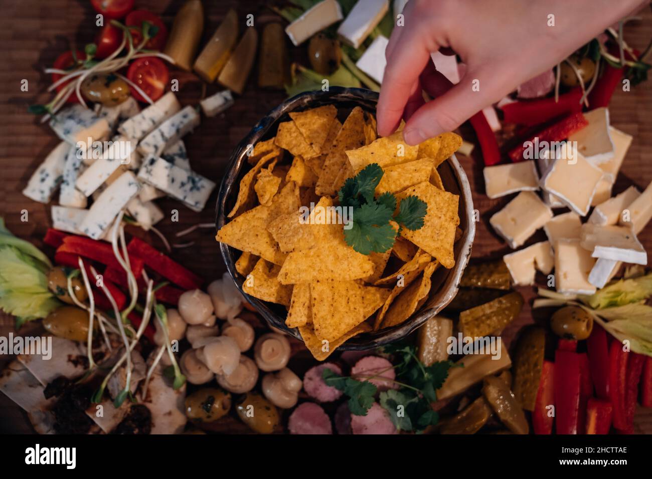 A picture of a hand holding nachos above the cold cuts board. Pickles ...