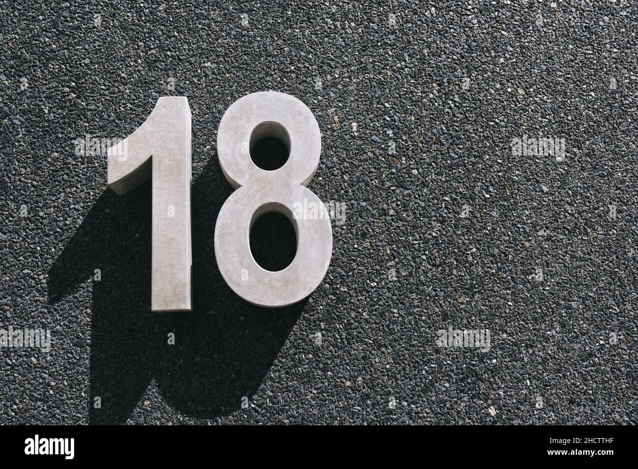 number 18 hanging of a black concrete wall Stock Photo - Alamy