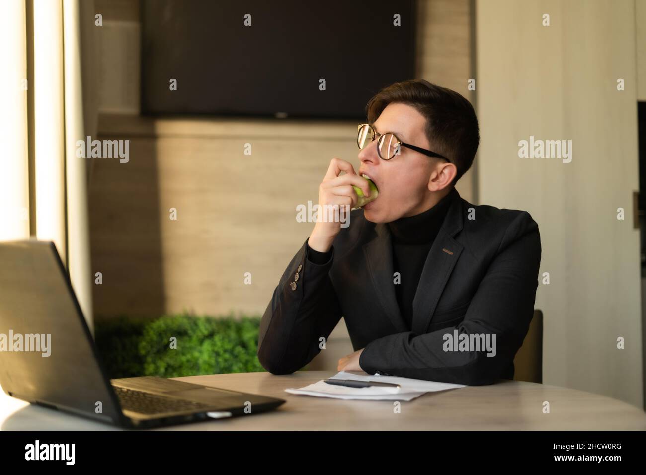 Businessman eating apple snack while sitting in office with laptop ...