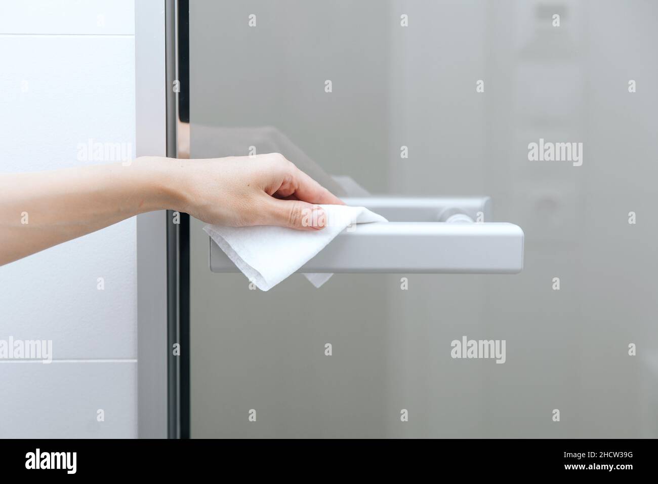 Cleaning glass door handles with an antiseptic wet wipe. Woman hand ...