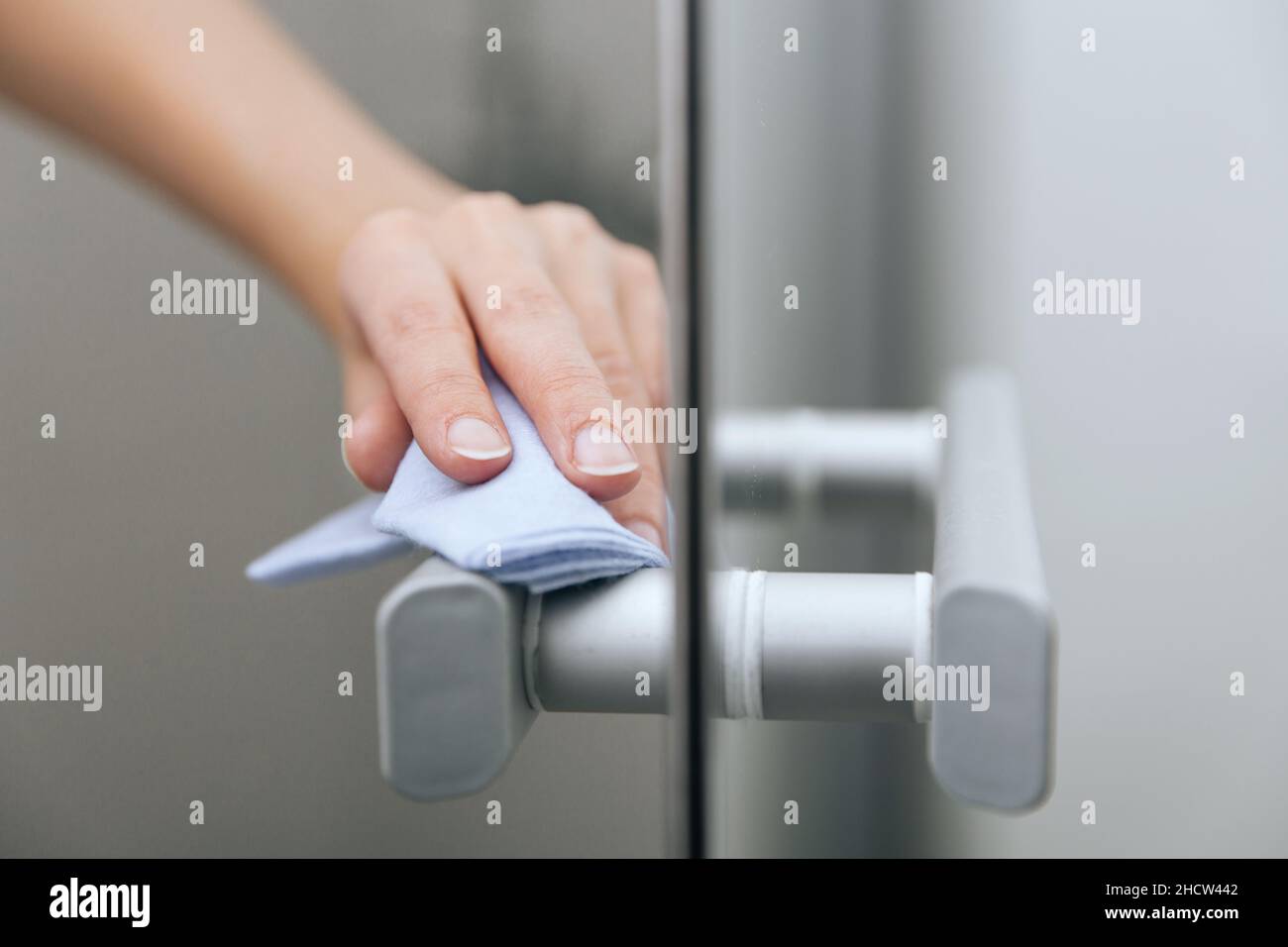 Cleaning glass door handles with an antiseptic wet wipe. Woman hand ...