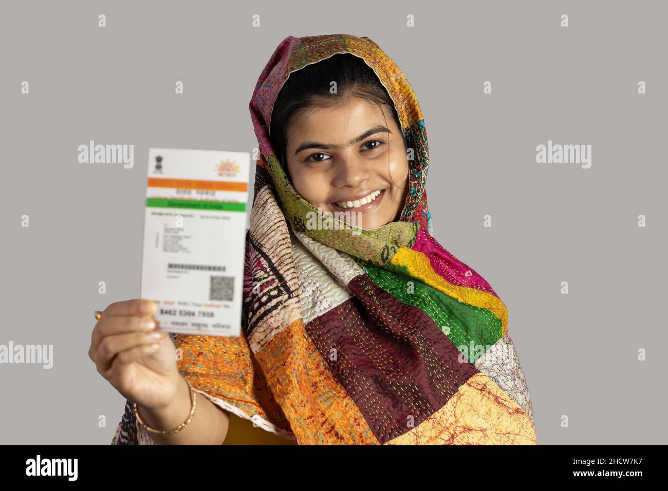An Indian young woman smiling with Aadhaar card in hand on white ...