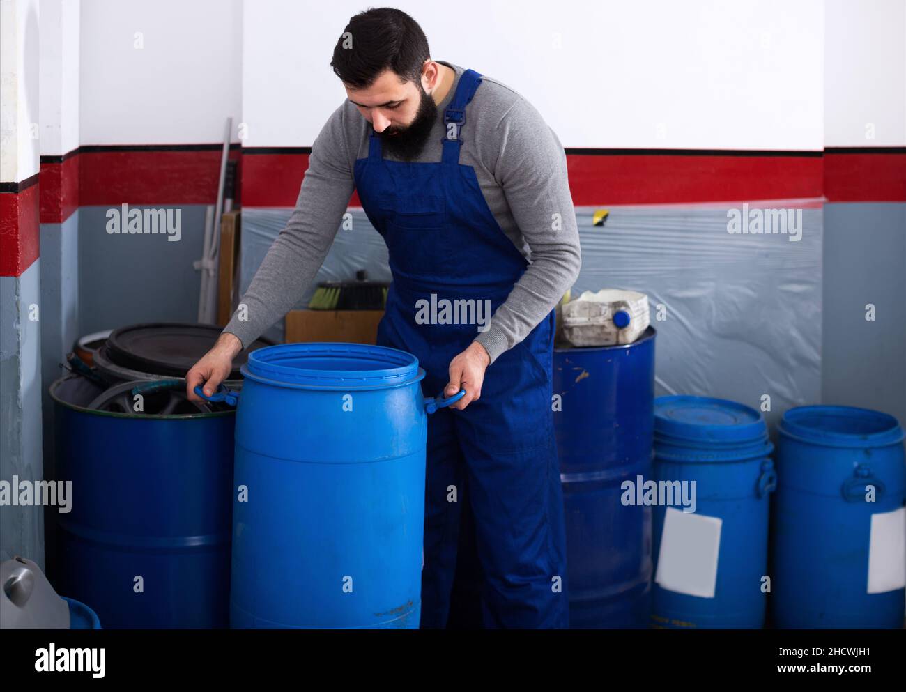 Smiling male worker picking up barrels to move Stock Photo - Alamy