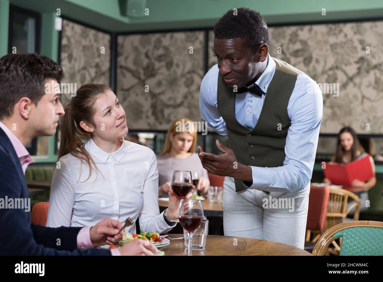 Positive couple talking with African American waiter Stock Photo - Alamy