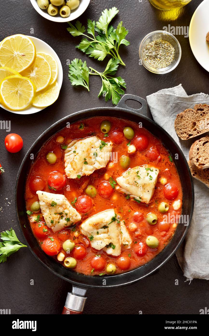 Cod stew with chickpeas, cherry tomatoes and olives in pan over dark ...