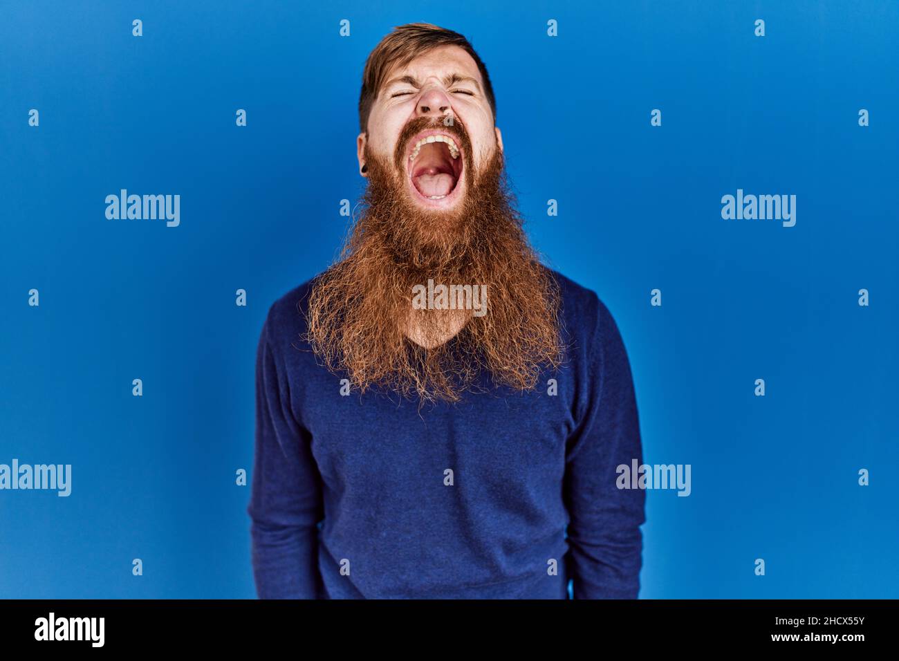 Redhead man with long beard wearing casual blue sweater over blue ...