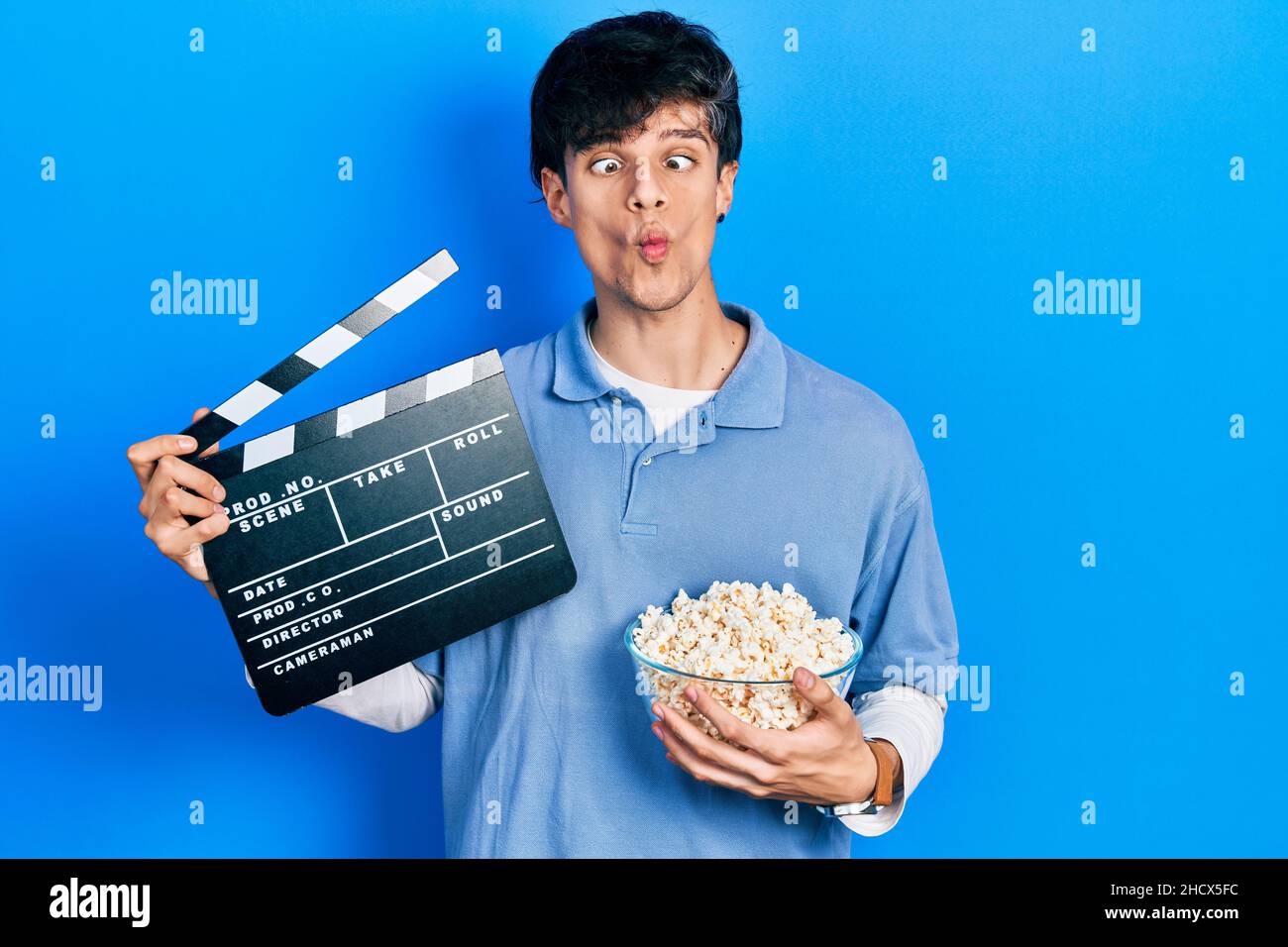 Handsome hipster young man eating popcorn holding cinema clapboard ...