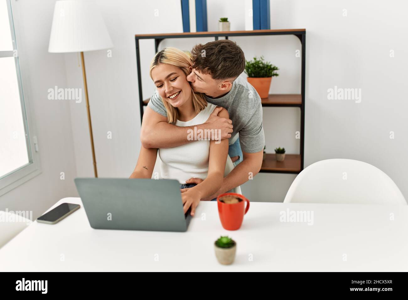 Young caucasian couple hugging and kissing using laptop sitting on the ...