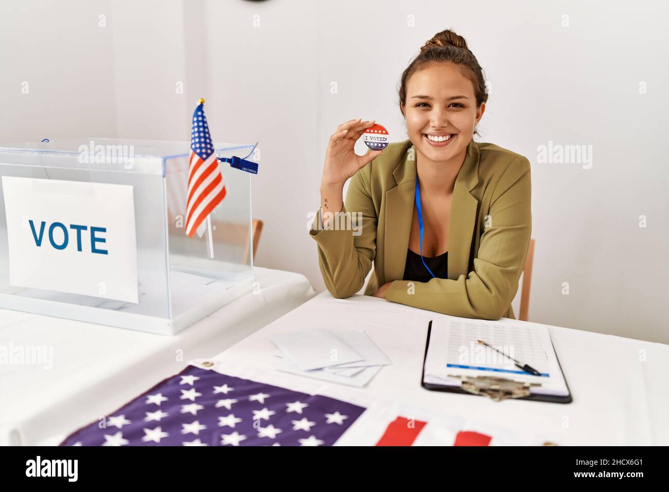 Beautiful hispanic woman at political campaign by voting ballot looking ...