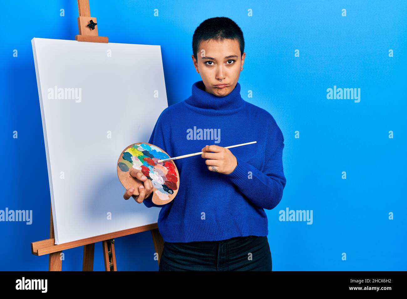 Beautiful hispanic woman with short hair holding paintbrush and palette ...